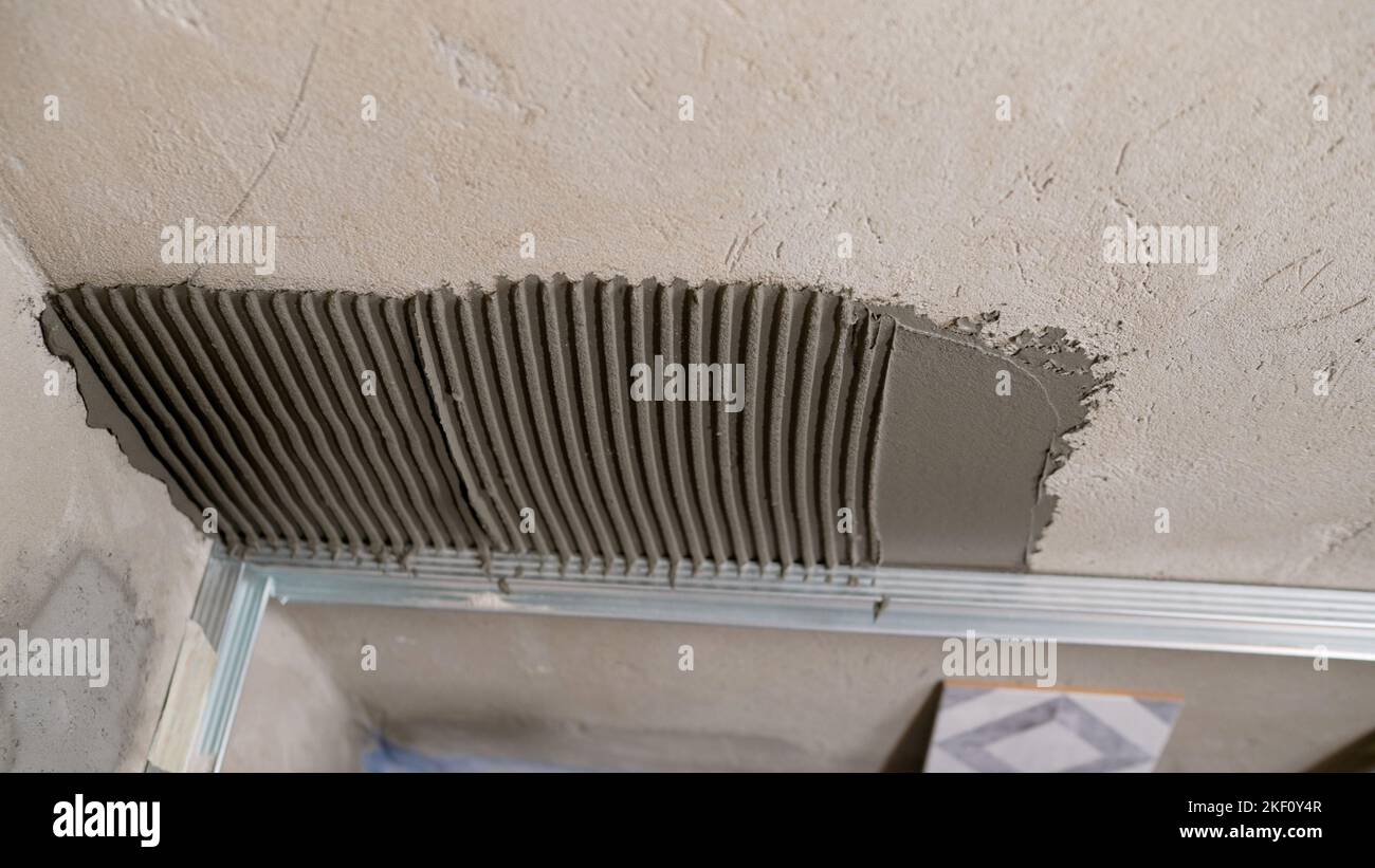 A worker applies glue to a wall to attach a plaster tile. The process ...