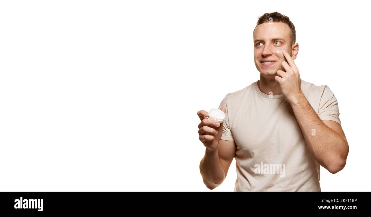 Portrait of young man with clear smooth face applying cream after ...