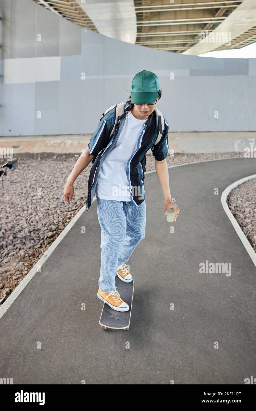 Vertical full length portrait of young Asian man skateboarding outdoors ...