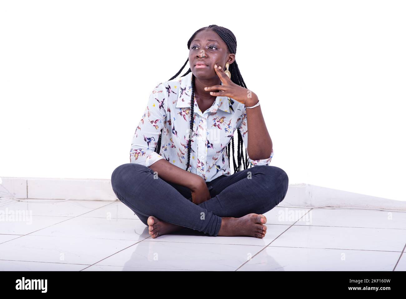 a beautiful young woman in a shirt sitting on the floor on a white ...