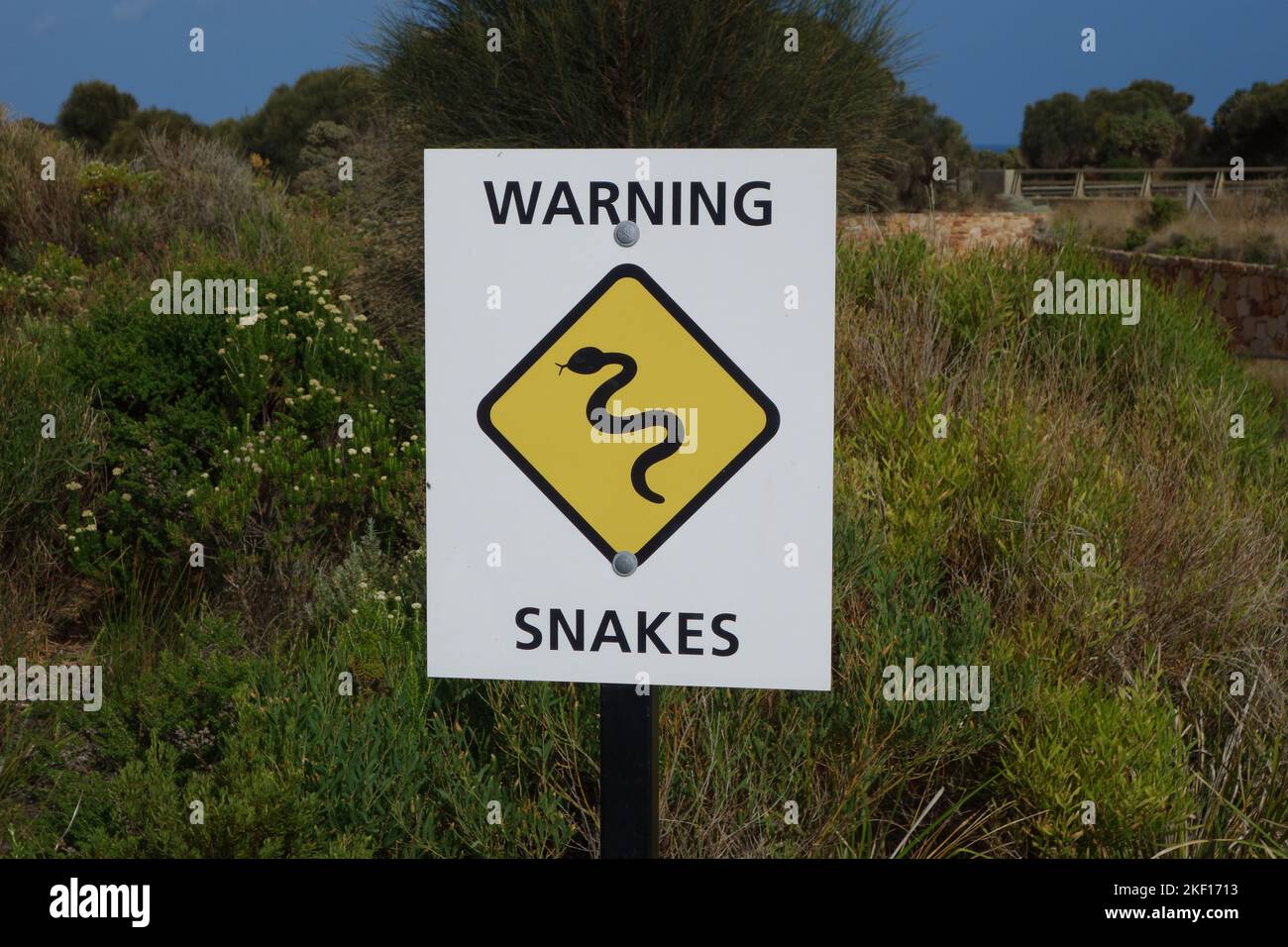 A white board with a yellow sign warning about snakes in a green area ...