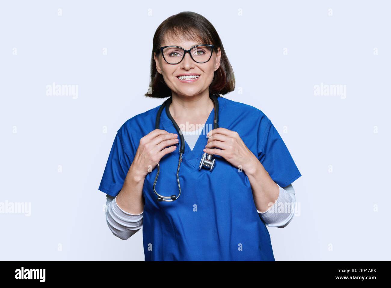 Portrait of middle aged doctor in uniform looking at camera on white ...