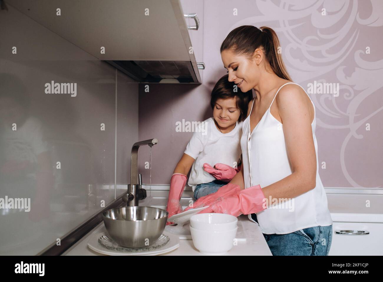 housewife mom in pink gloves washes dishes with her son by hand in the ...