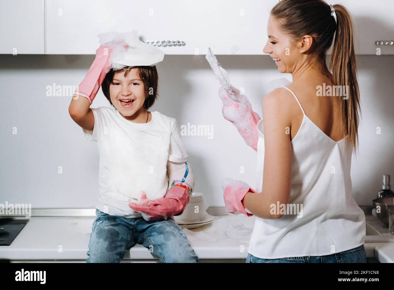 housewife mom in pink gloves washes dishes with her son by hand in the ...