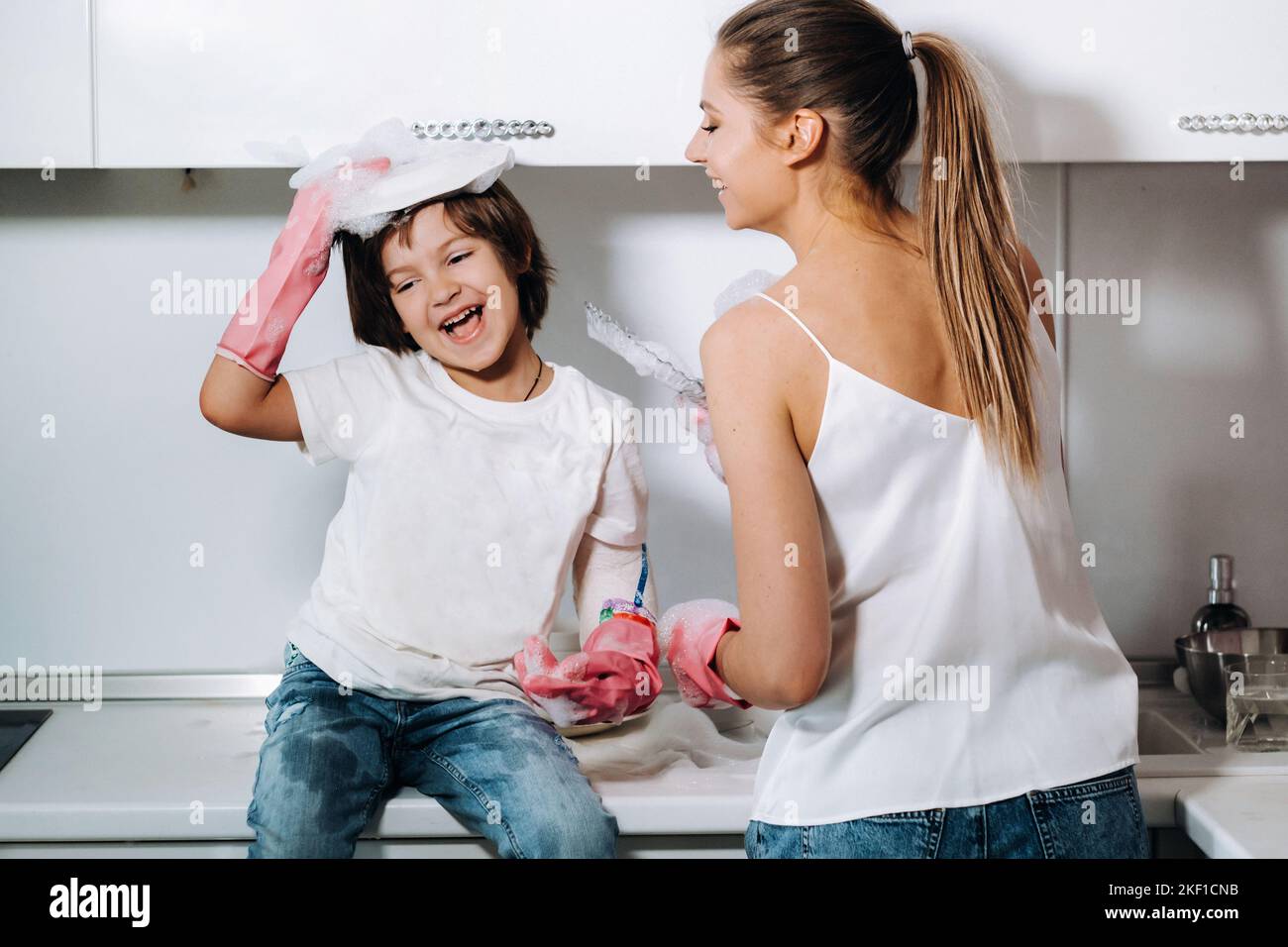 housewife mom in pink gloves washes dishes with her son by hand in the ...