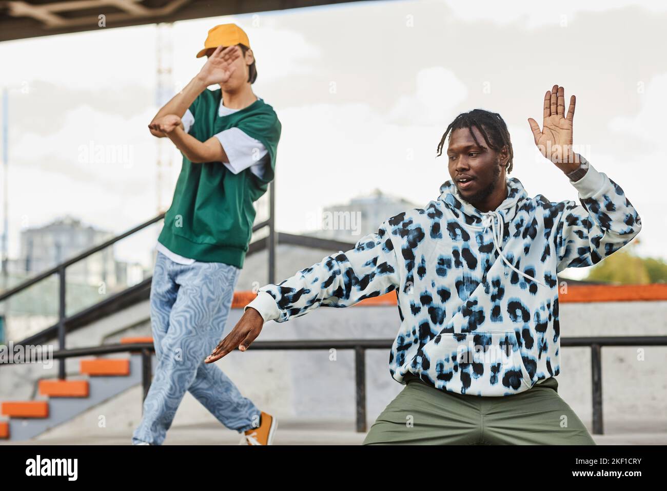 Portrait of two young men dancing outdoors in urban area and wearing ...
