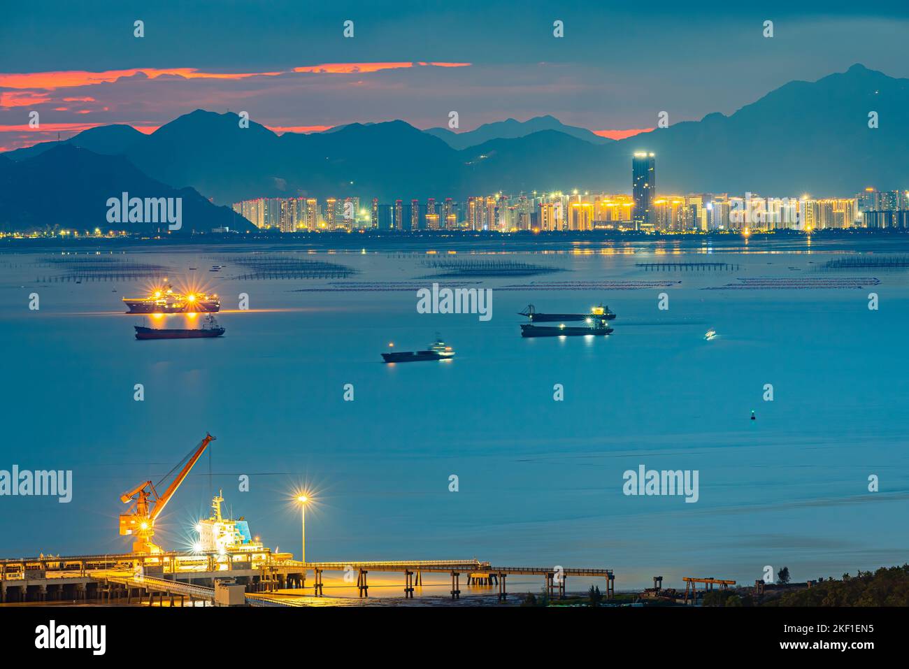 A sunset view of a harbor with an illuminated city in the background ...