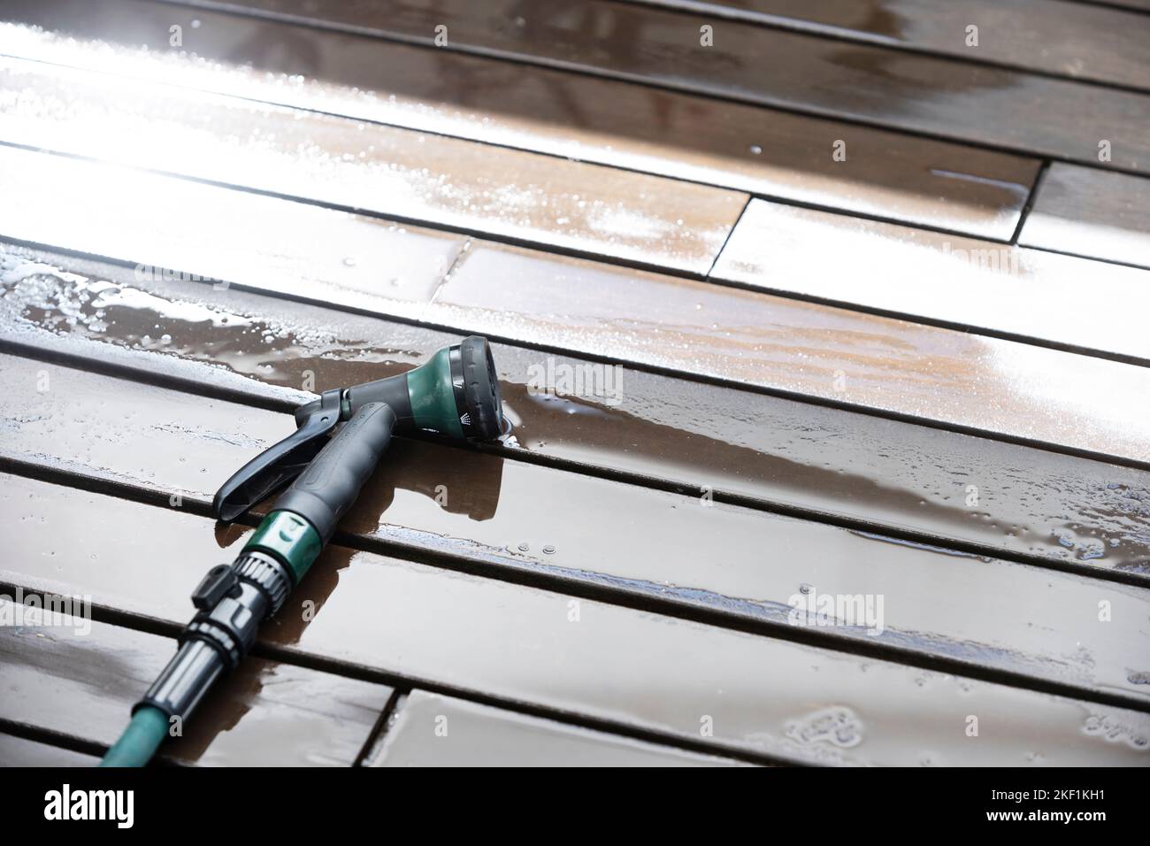 Sprinkler tap from a hose on a terrace with wet wooden floors Stock ...