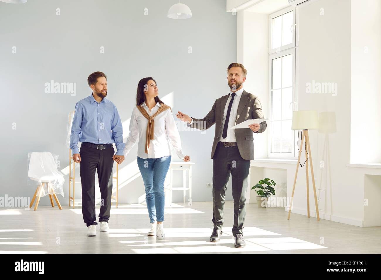 Real estate agent is giving a young family a tour around a big house or ...