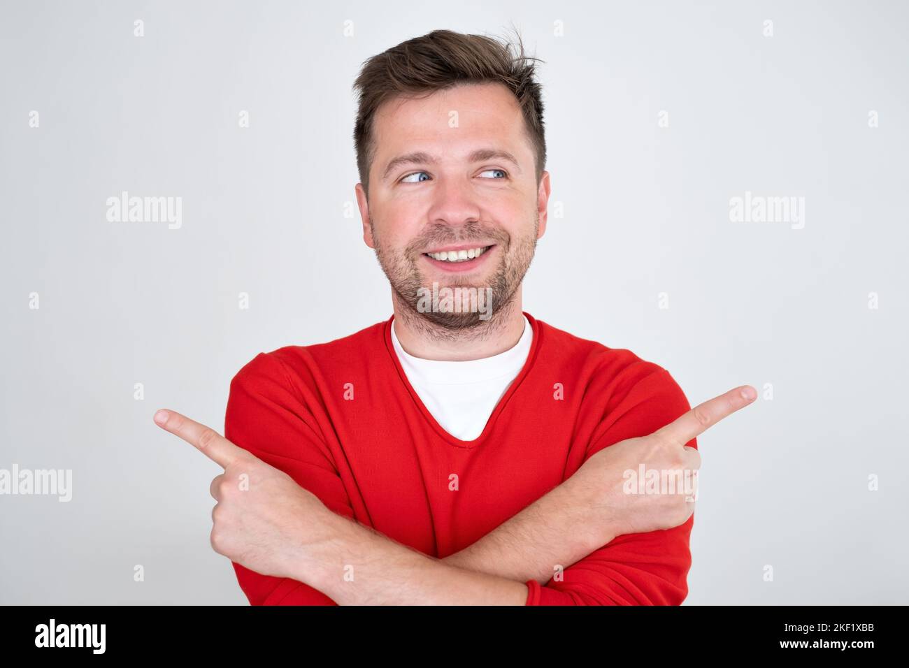 Smiling man standing with crossed hands and pointing to copy space on ...