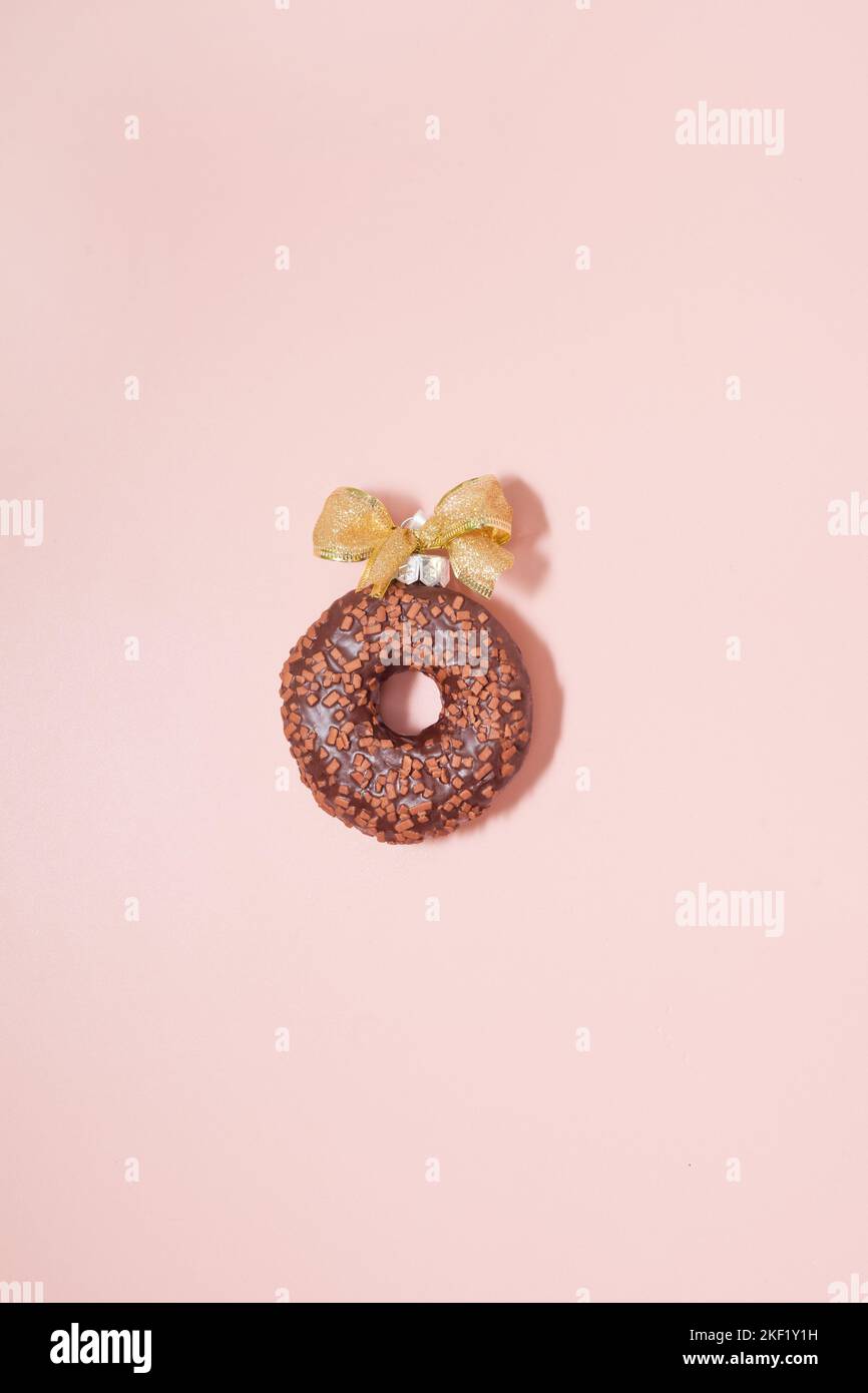 chocolate donut with golden bow on pink background. single glazed ball ...