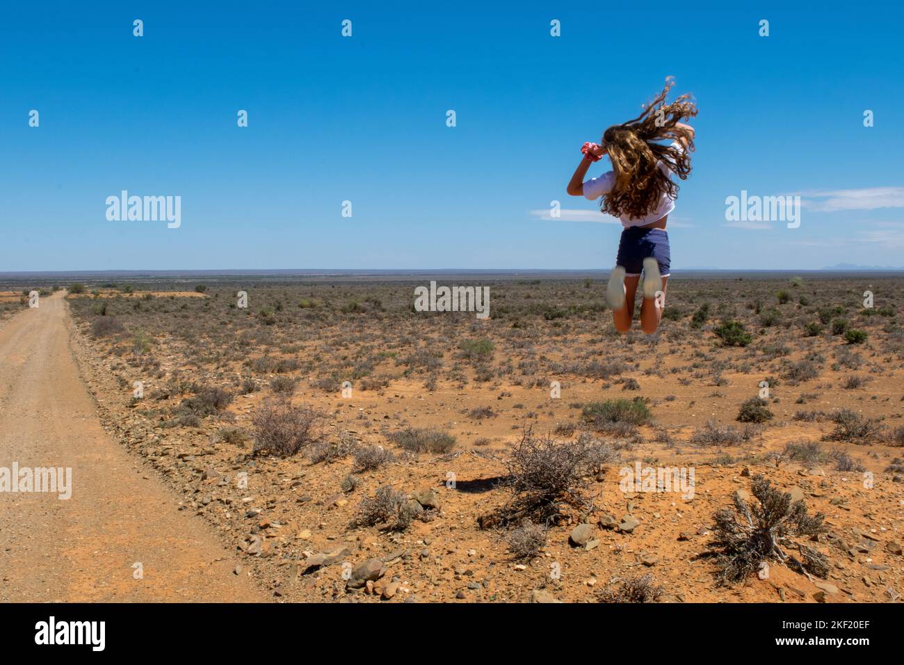 A back view of female jumping over field with growing bushes in Africa ...