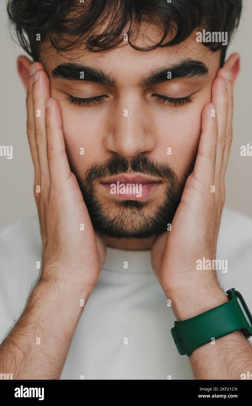 Close-up portrait of a handsome man keeping his eyes closed, touching ...