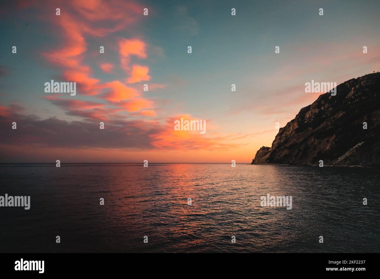 A beautiful scene of red sunset sky reflecting on sea with rocky cliffs ...