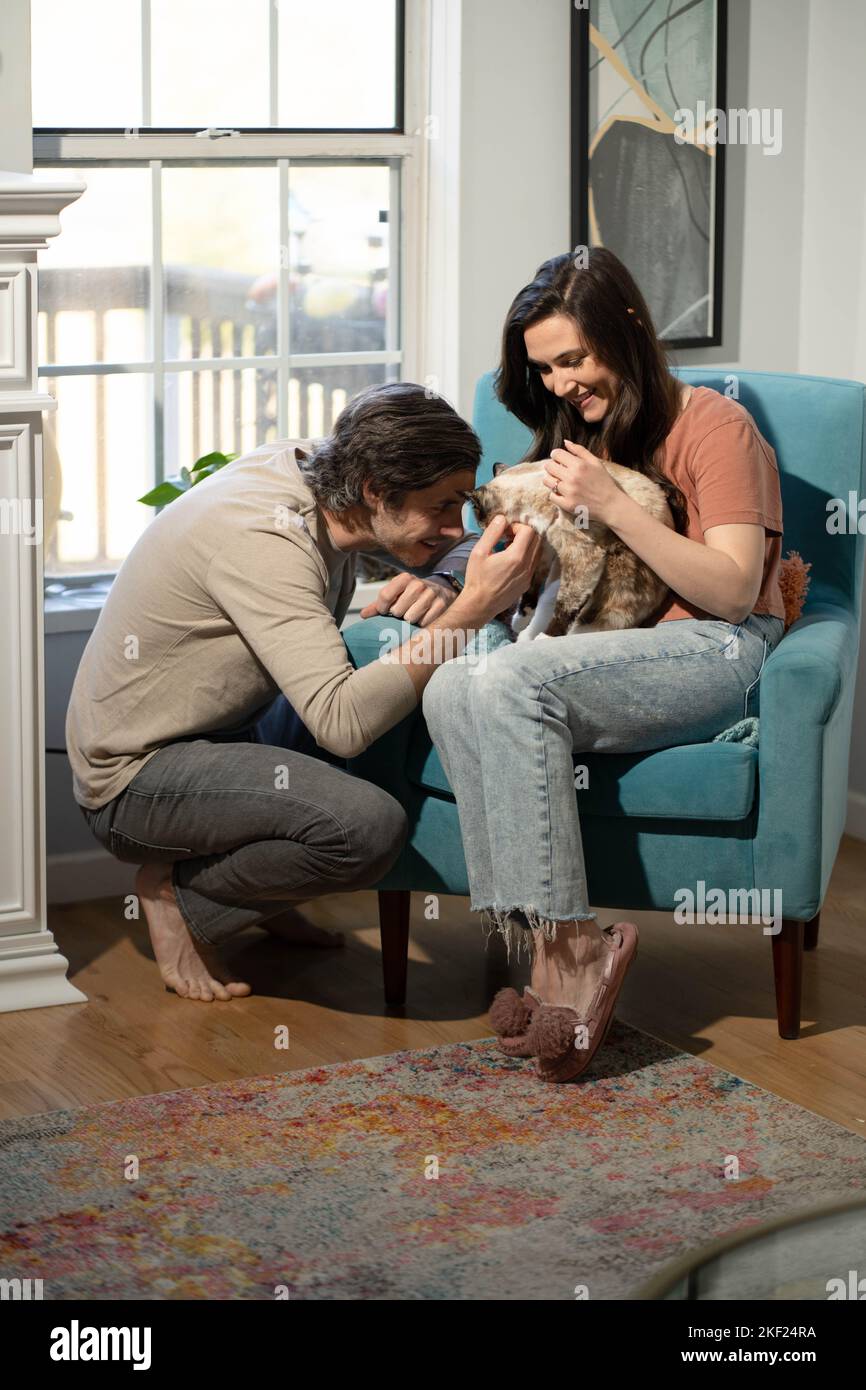 A man and woman in their living room with their cat, lovingly snuggling ...