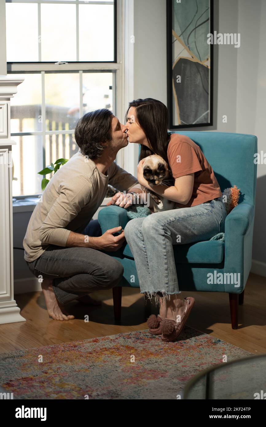 A man and woman in their living room with their cat, lovingly snuggling ...