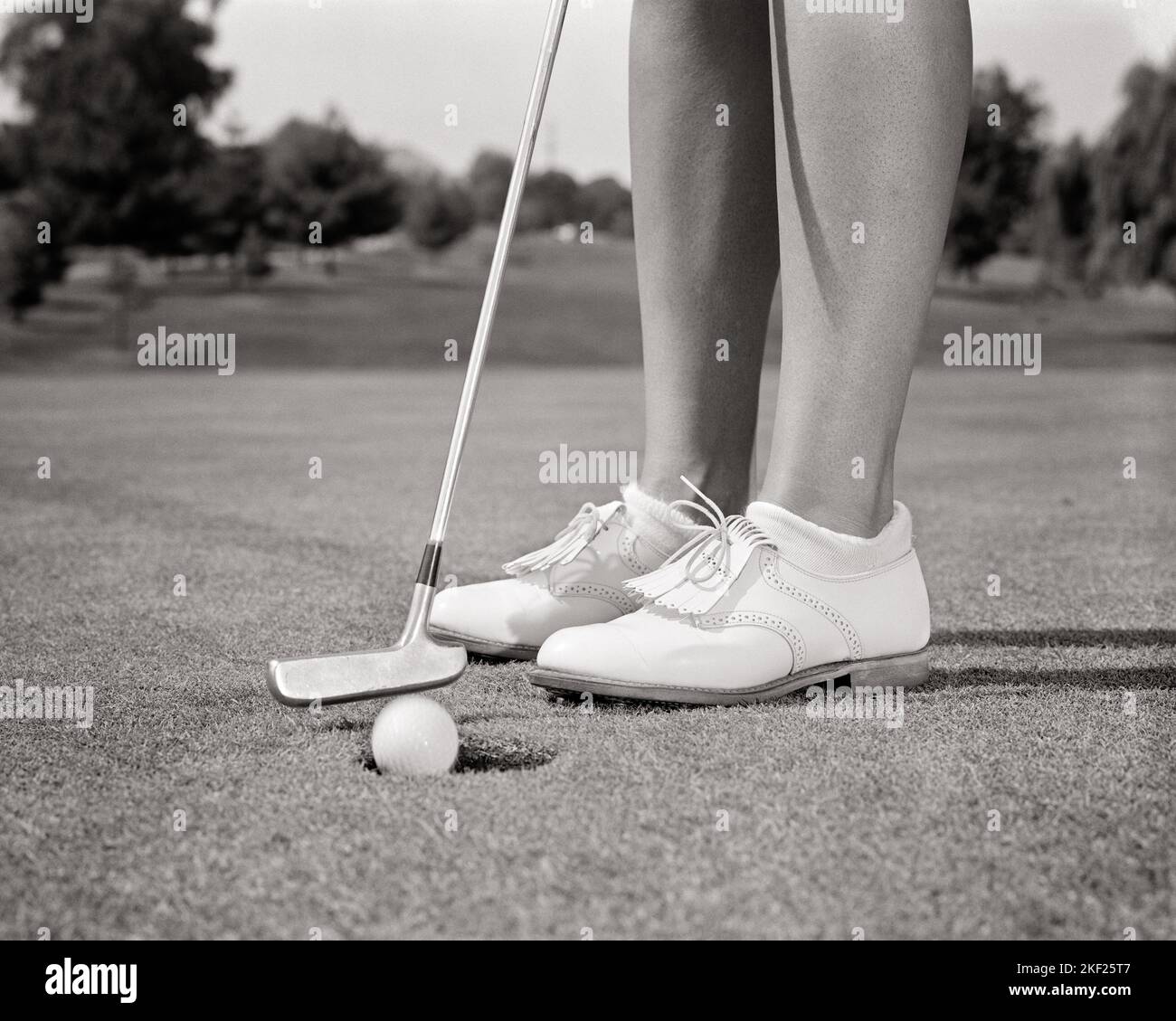 1960s CLOSE-UP OF FEMALE LEGS WEARING WHITE GOLF SHOES AND CLUB PUTTER ...