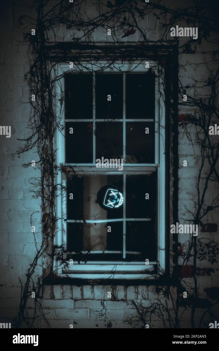 A LED, spooky Halloween mask, peeking from an old window surrounded ...