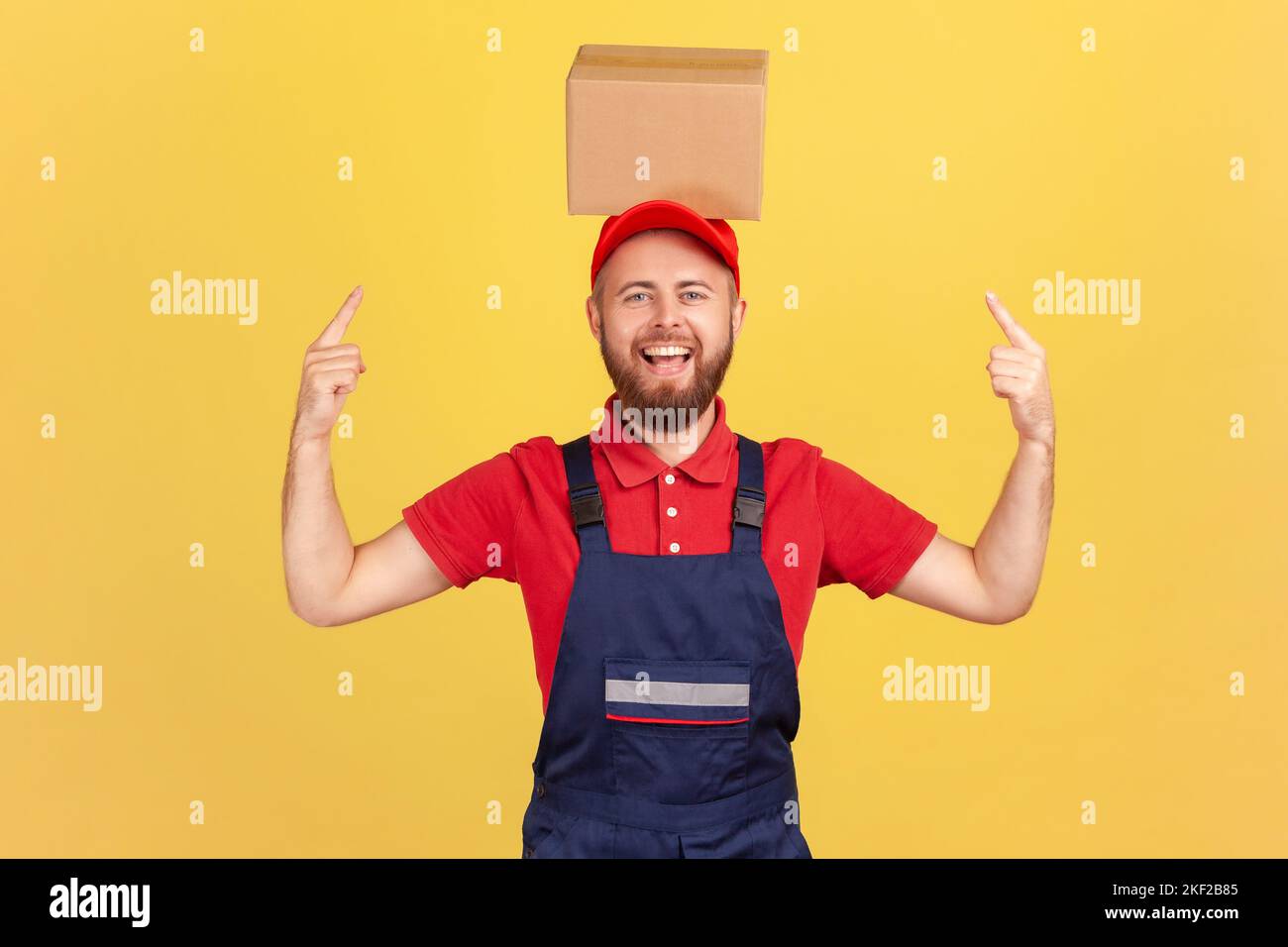 Portrait of excited courier man wearing blue uniform standing pointing ...