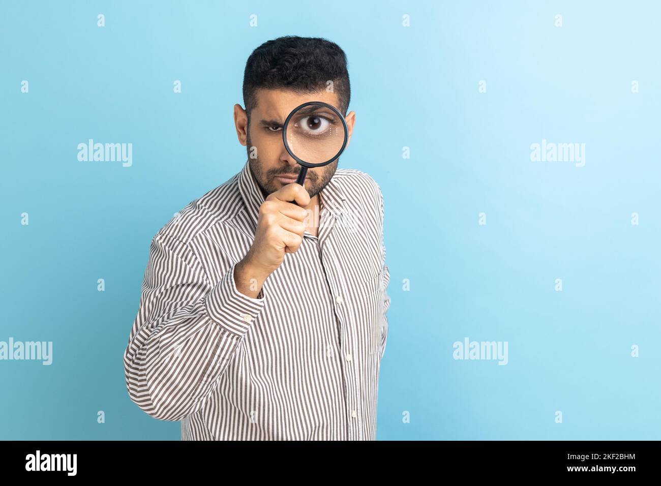 Serious bearded man holding magnifying glass and looking at camera with ...