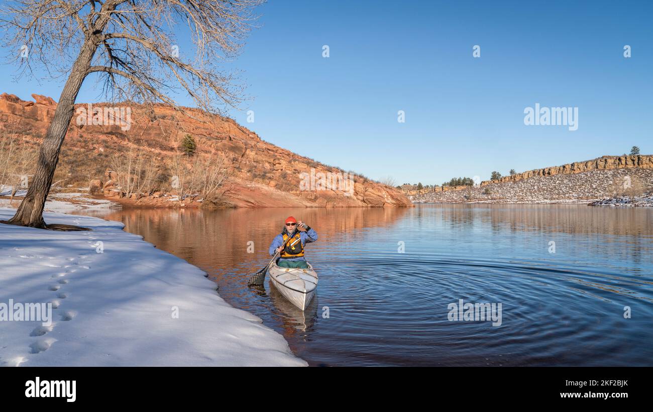 senior male wearing life jacket is paddling expedition canoe in winter ...