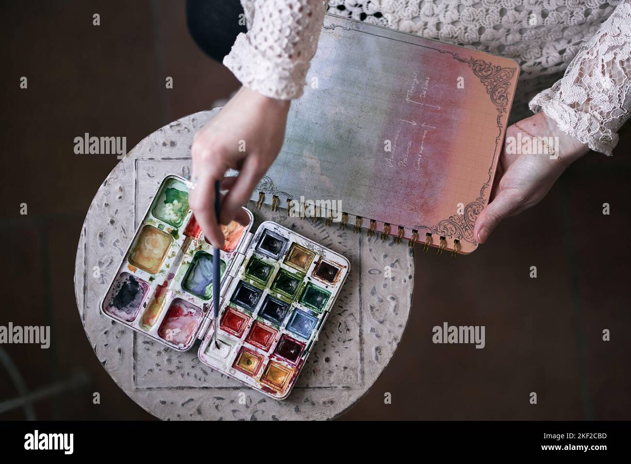 closeup of a case of watercolors of many colors and a hand holding a ...