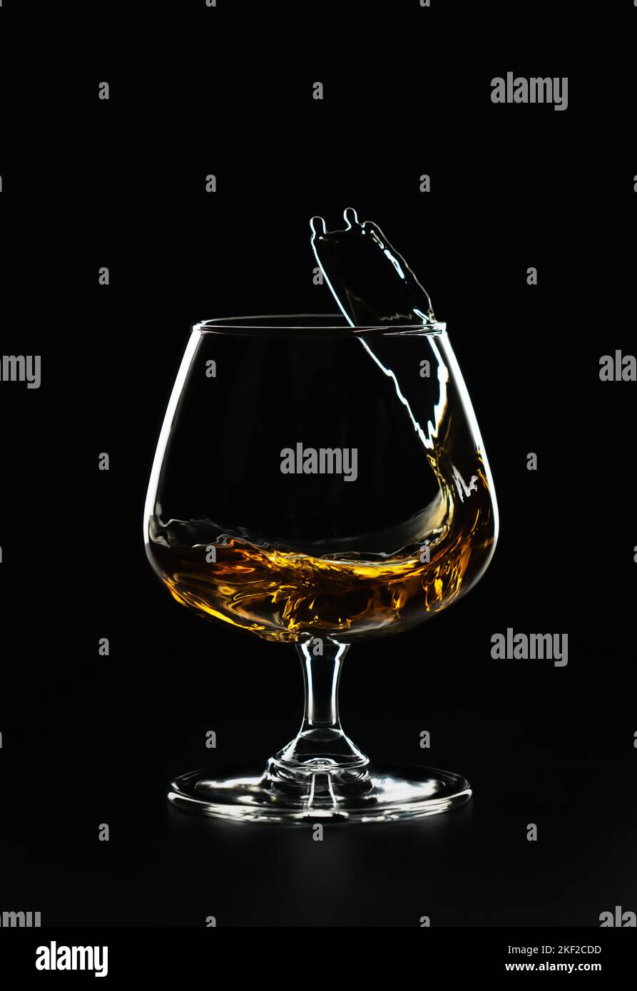 A splash of cognac in a glass on a black background Stock Photo - Alamy