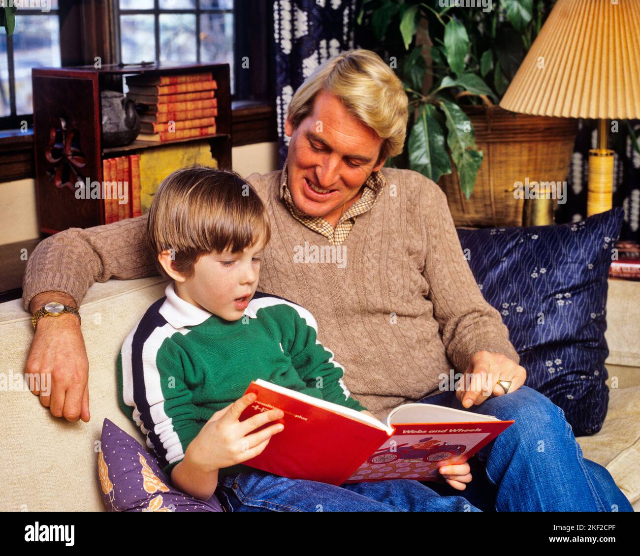 1970s 1980s BLONDE MAN FATHER SITTING ON COUCH READING A BOOK WITH ...