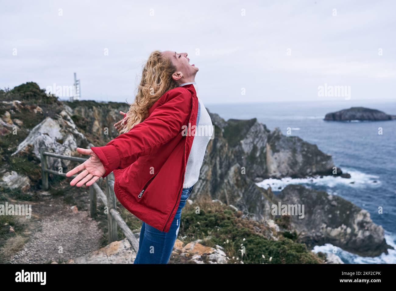 blonde caucasian young woman in red jacket and blue pants standing with ...
