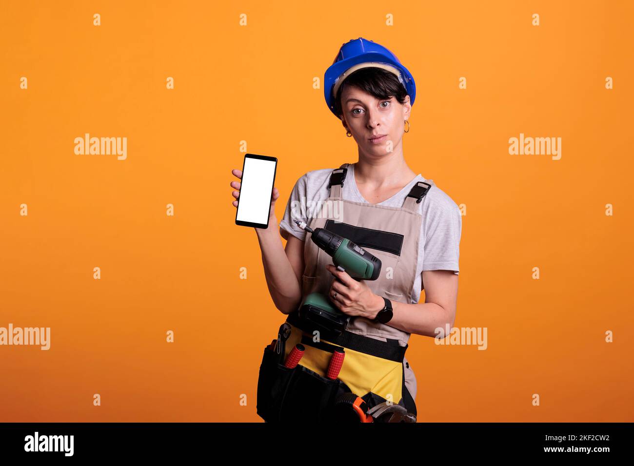 Female contractor pointing drilling gun at empty white screen on mobile ...