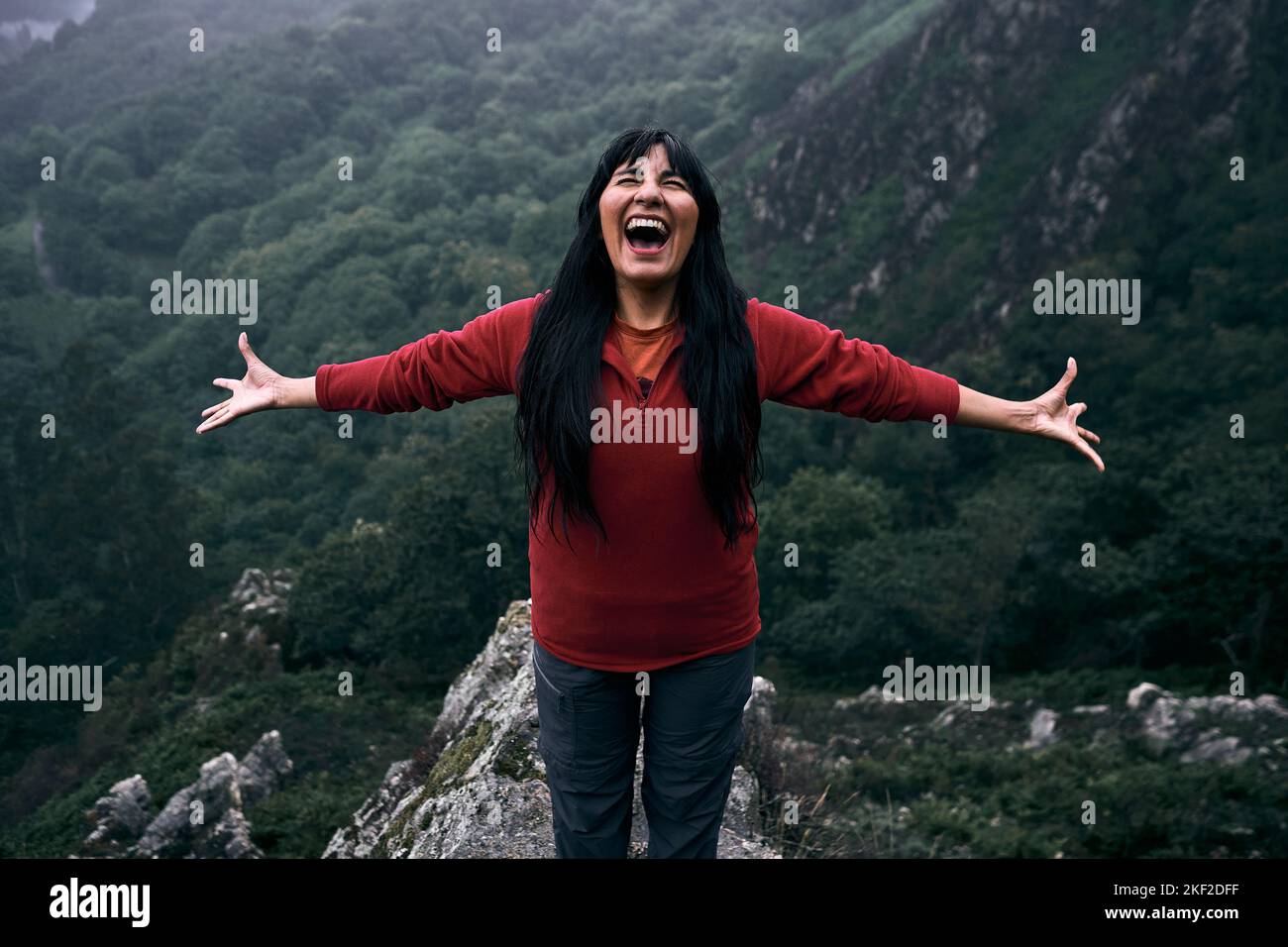brunette latin girl with red sweater climbing on a big stone on the top ...