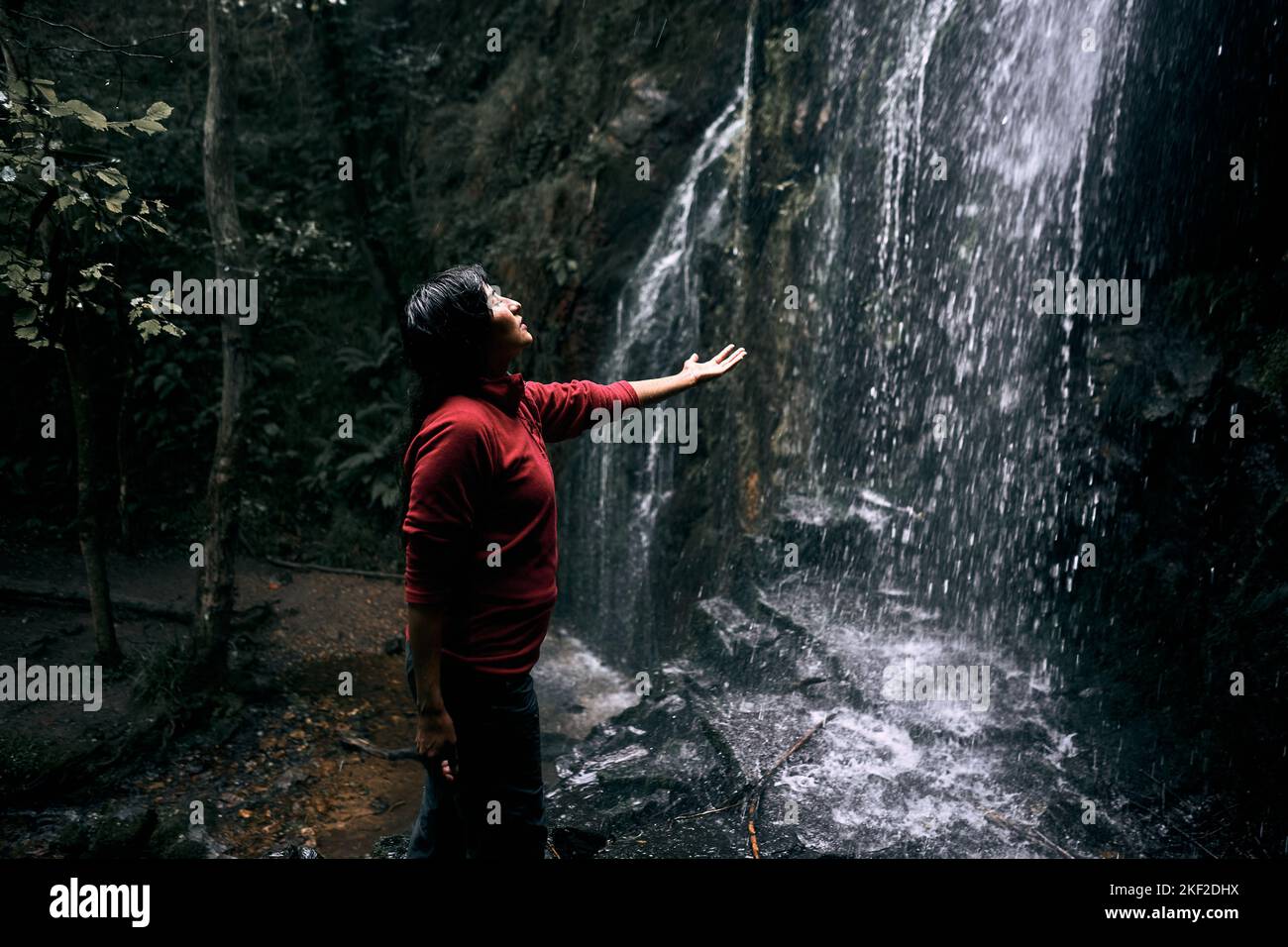 latin young woman with long hair standing by waterfall with eyes closed ...