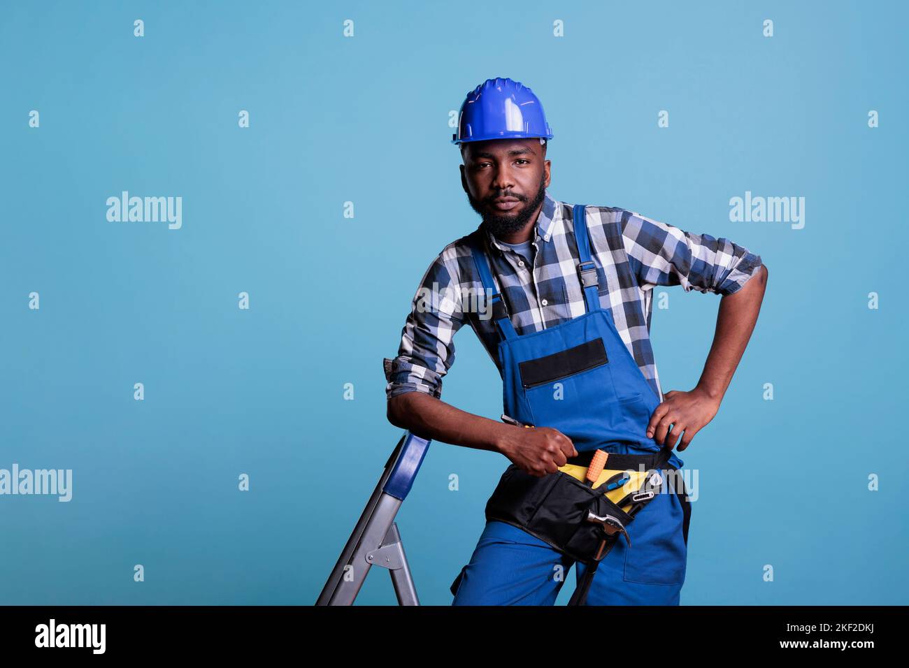 Serious builder leaning on ladder wearing coveralls and protective ...