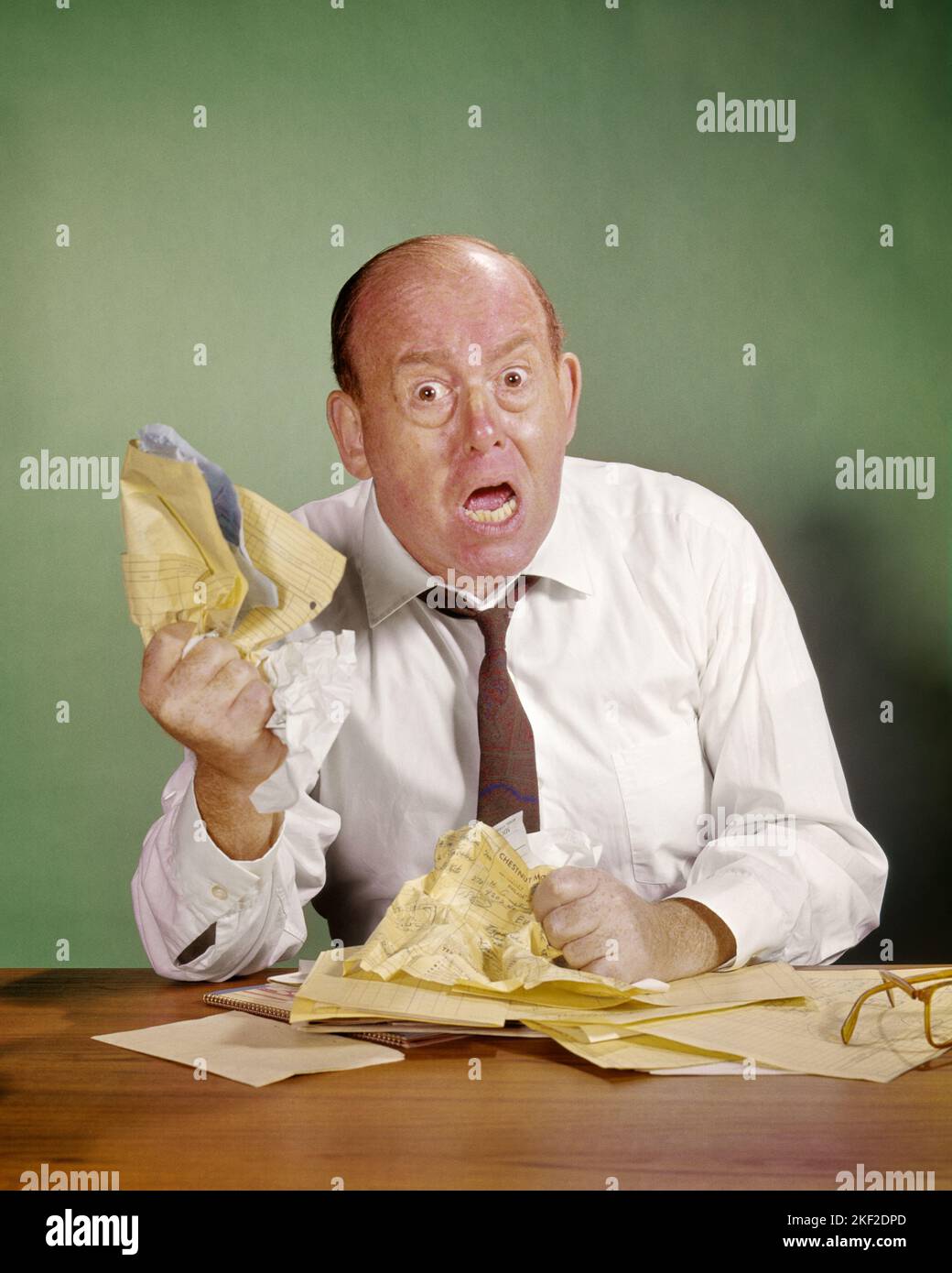 1960s ANGRY FRUSTRATED MAN CRUMPLING AND TEARING PAPERS AT DESK STUDIO ...