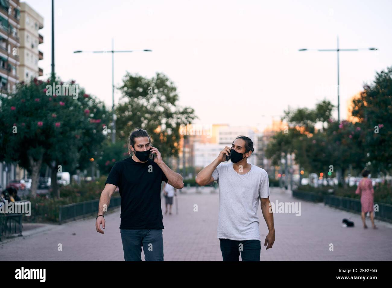 two caucasian boys walking down the street side by side talking on ...