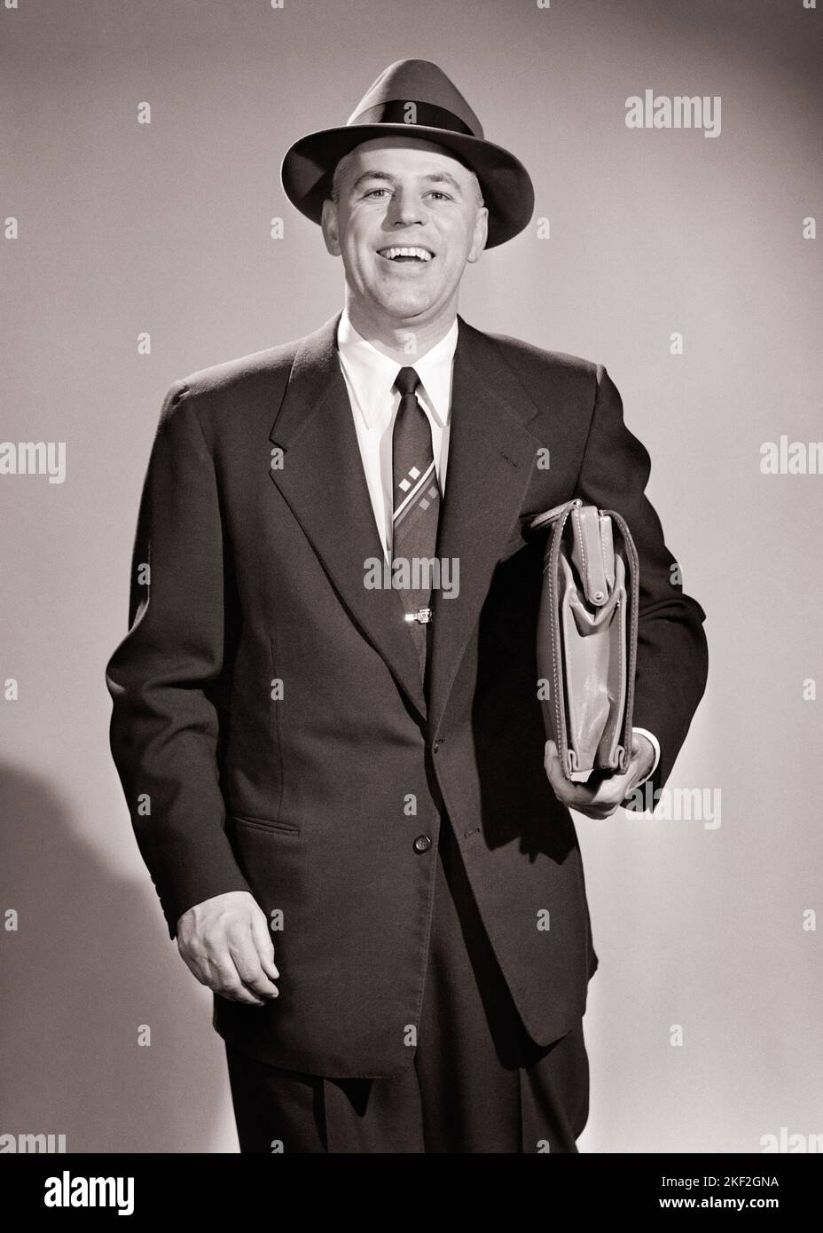 1950s SMILING SALESMAN LOOKING AT CAMERA WEARING BUSINESS SUIT HOLDING ...