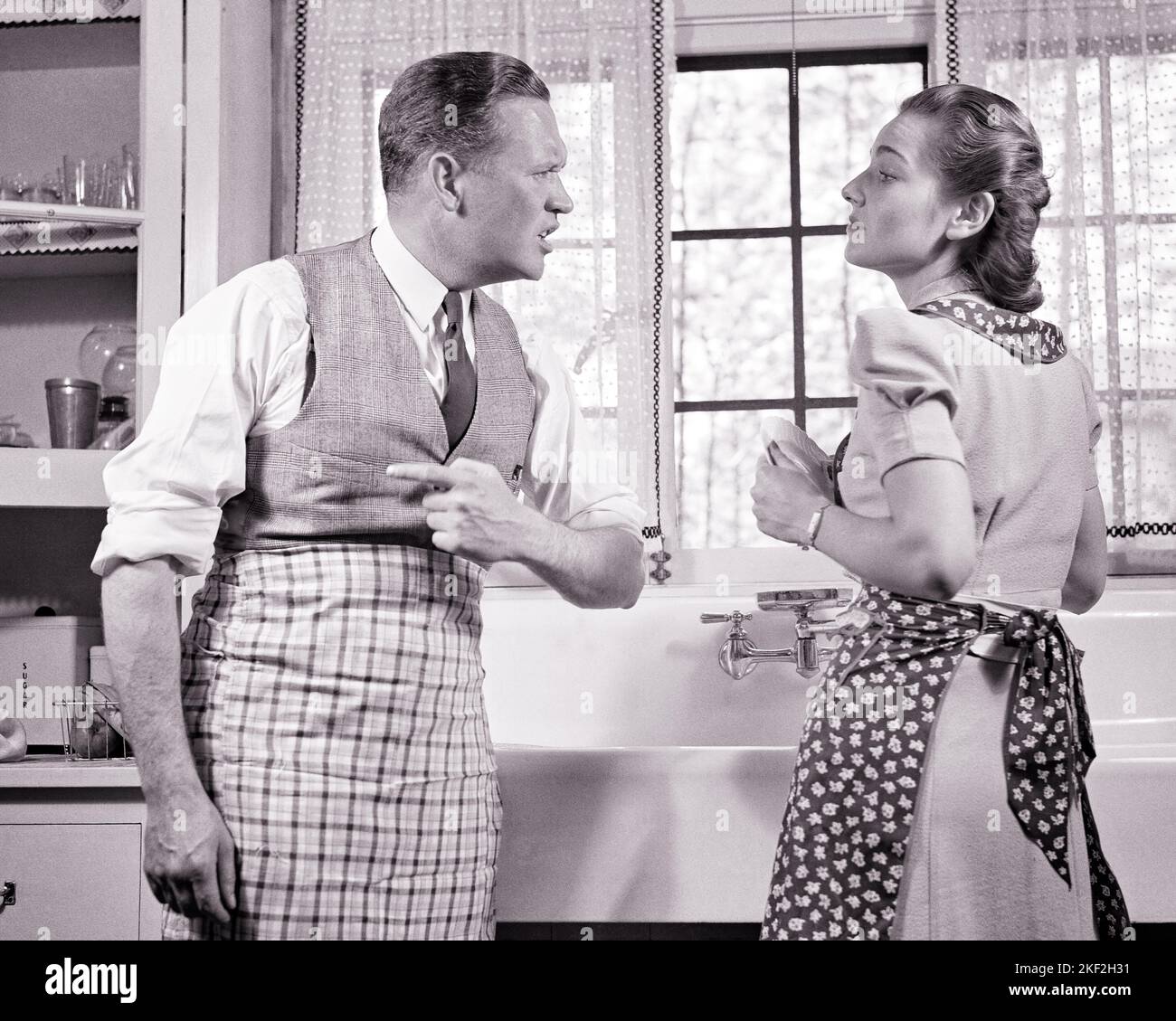 1930s HUSBAND & WIFE IN KITCHEN BOTH WEARING APRONS ARGUING AT SINK MAN ...