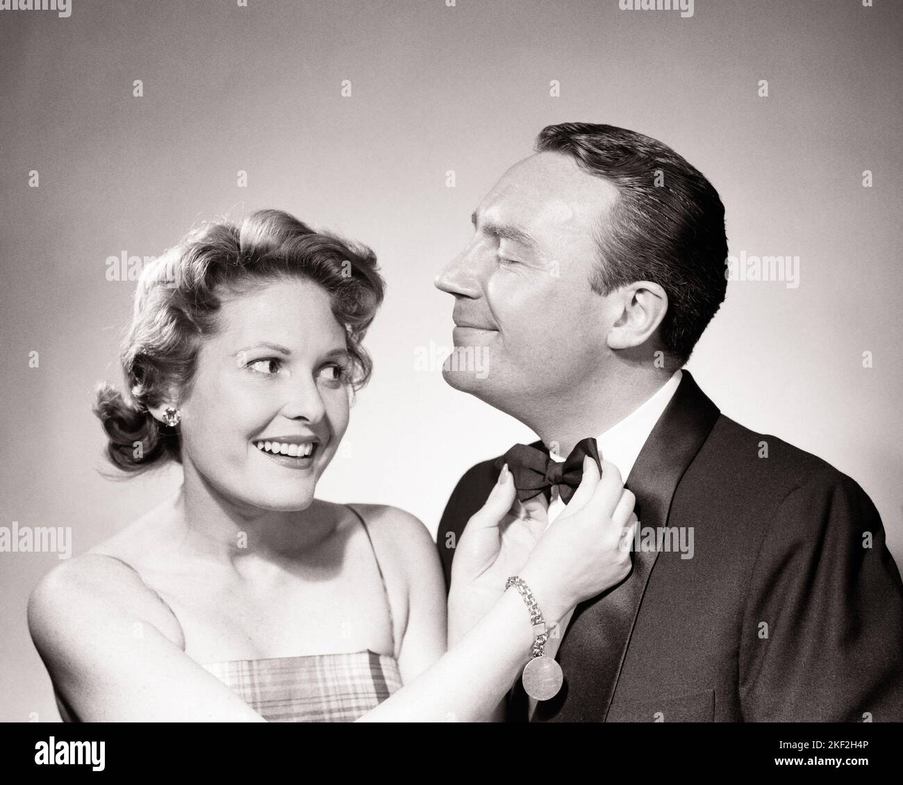 1950s GOING OUT FOR THE EVENING WOMAN FIXING MAN’S BOW TIE SHE IS ...