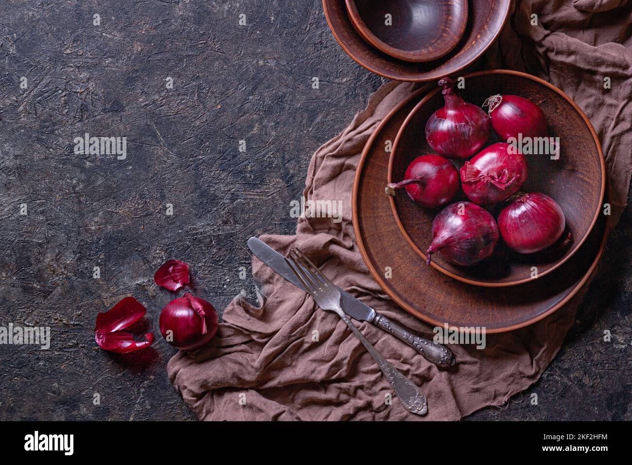 Ripe red onion bulbs in a clay bowl on a stone surface, flat lay, low ...
