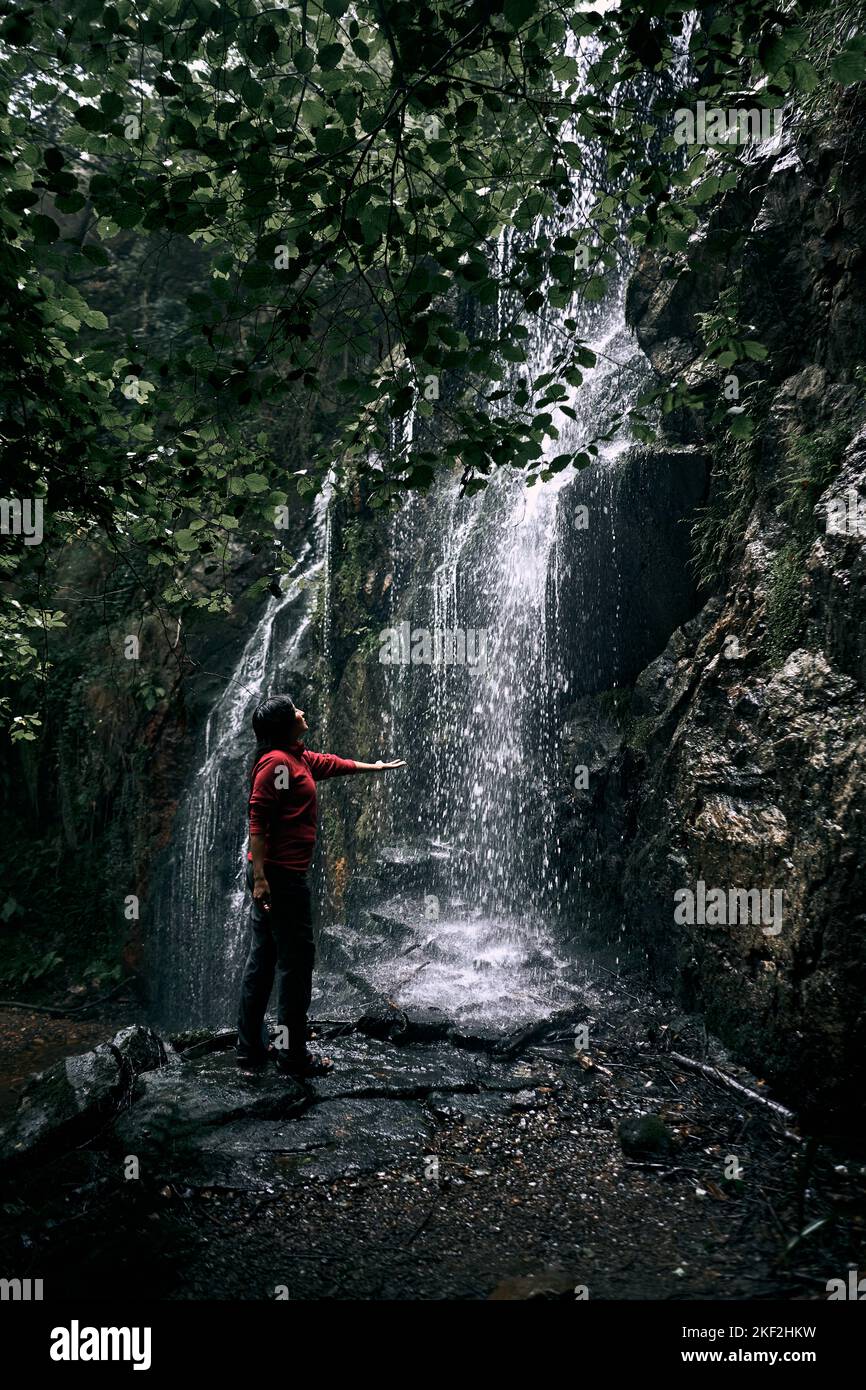 latin girl with left arm outstretched and palm up wet by waterfall ...