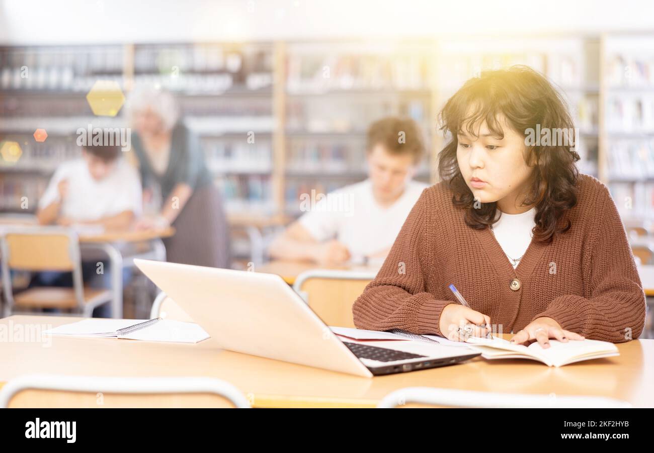 Schoolgirl studies on a laptop and writes notes in a copybook Stock ...