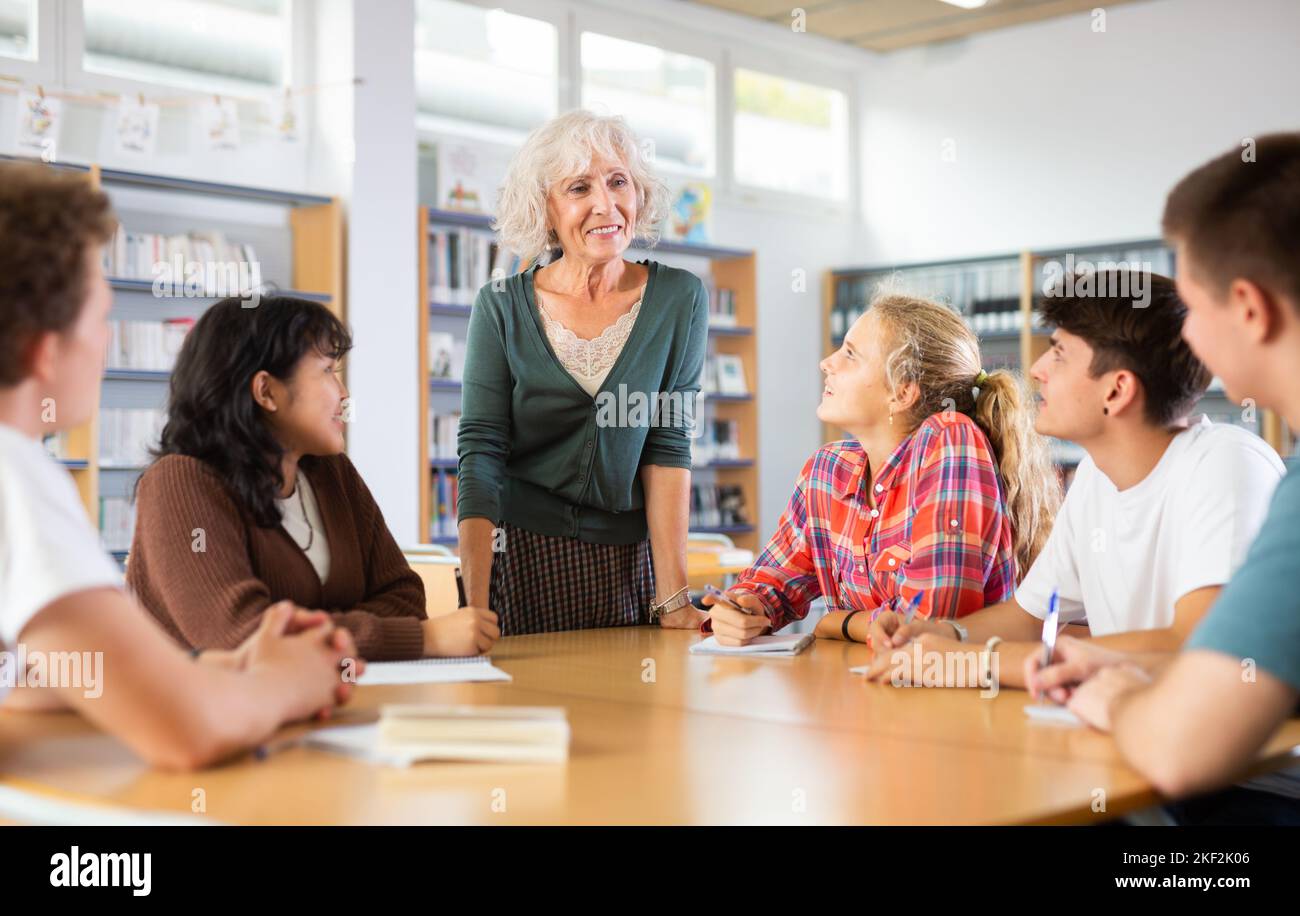 Group of schoolchildren with a female teacher in the library ...