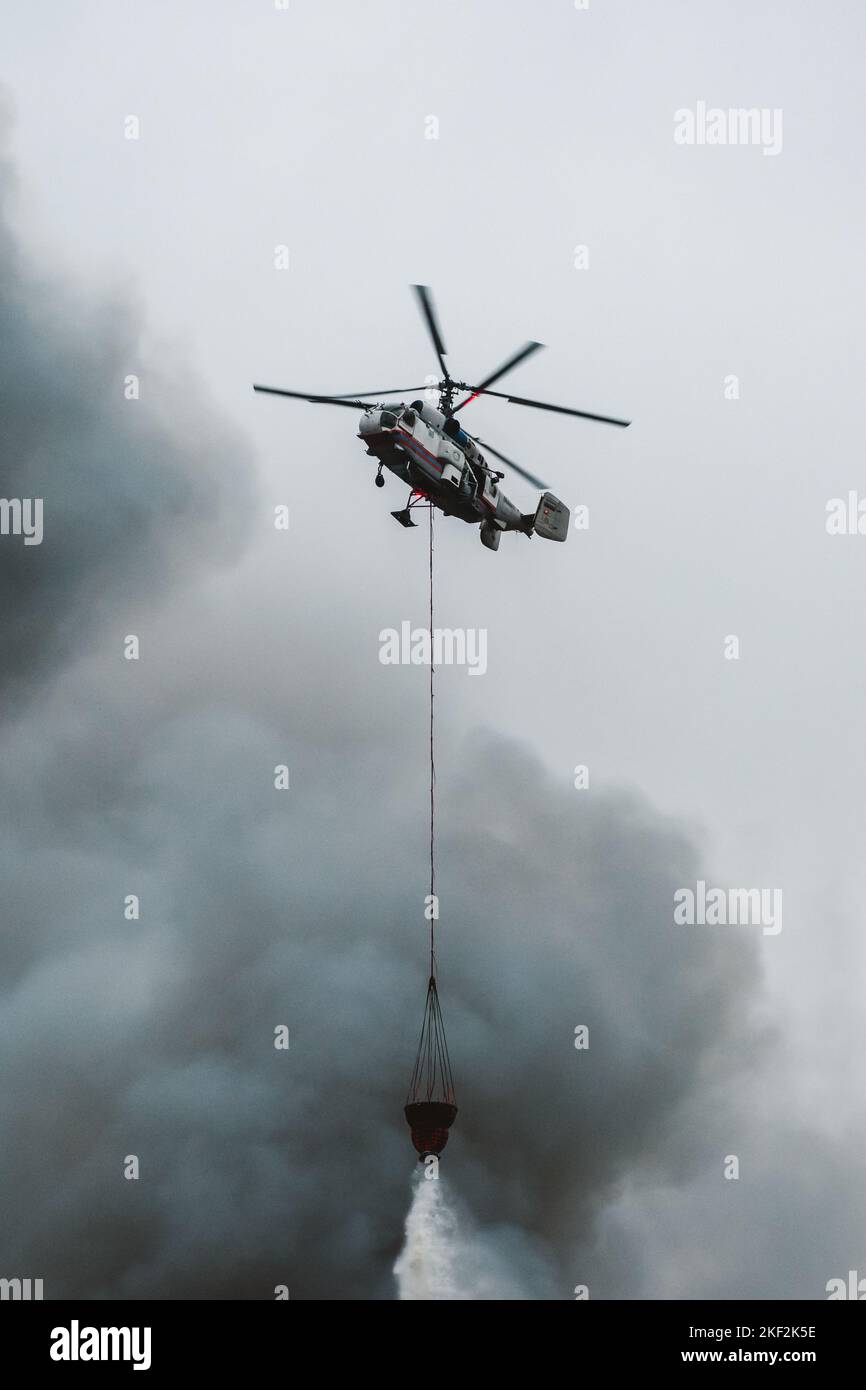 A fire helicopter carries a container of water to extinguish a fire in ...