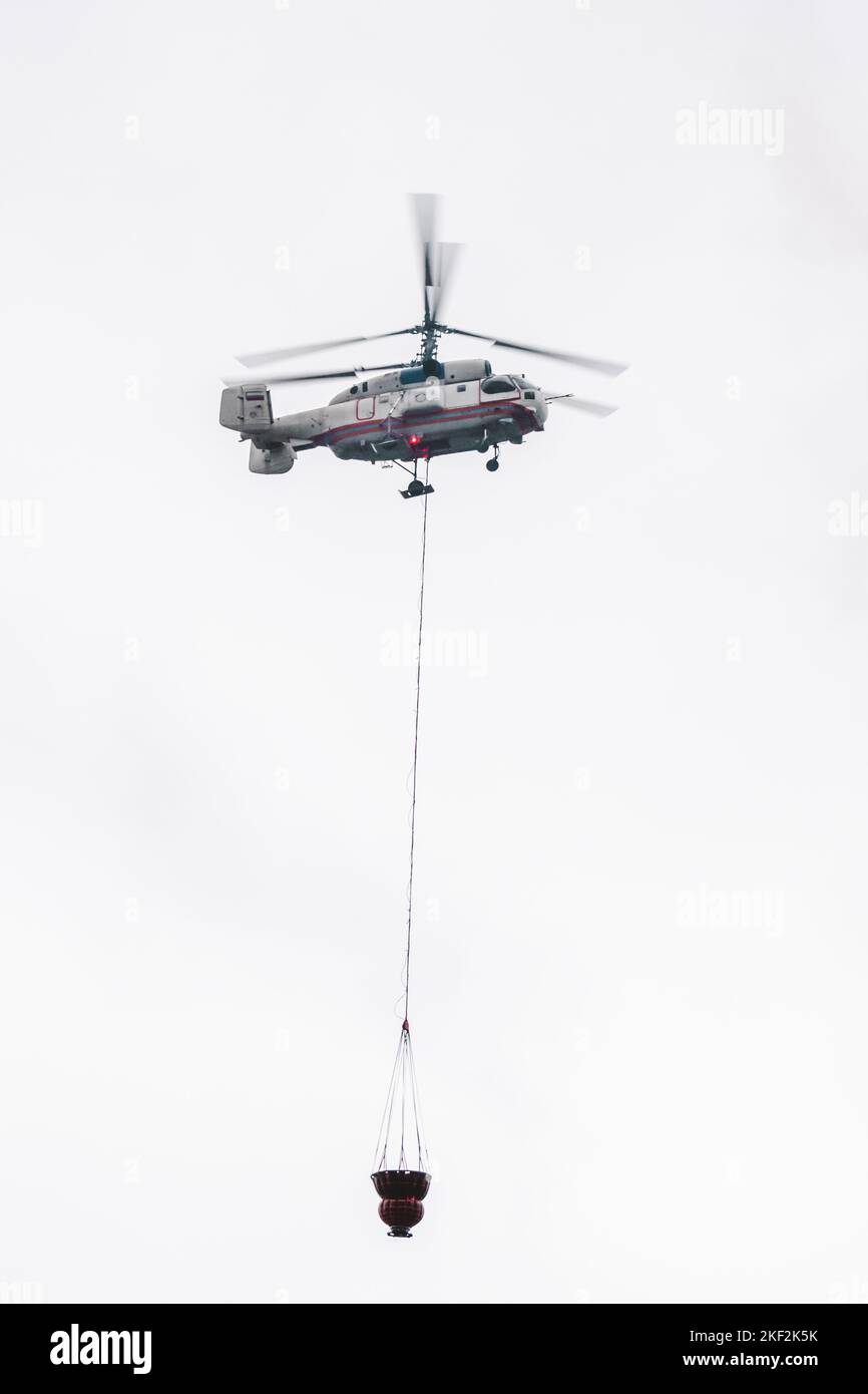 A fire helicopter carries a container of water to extinguish a fire in ...