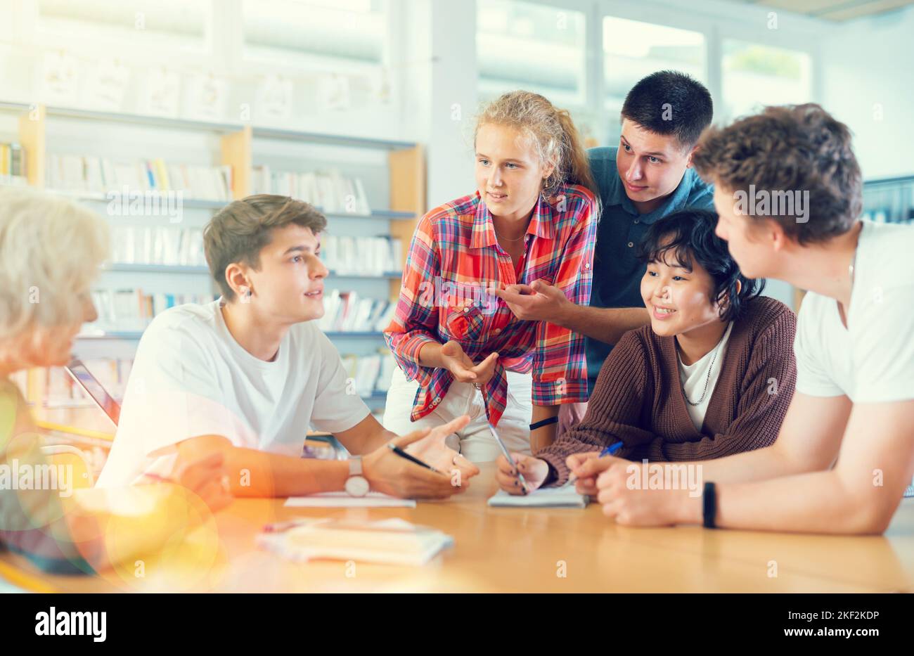 Positive teenage students working and discussing in groups in library ...