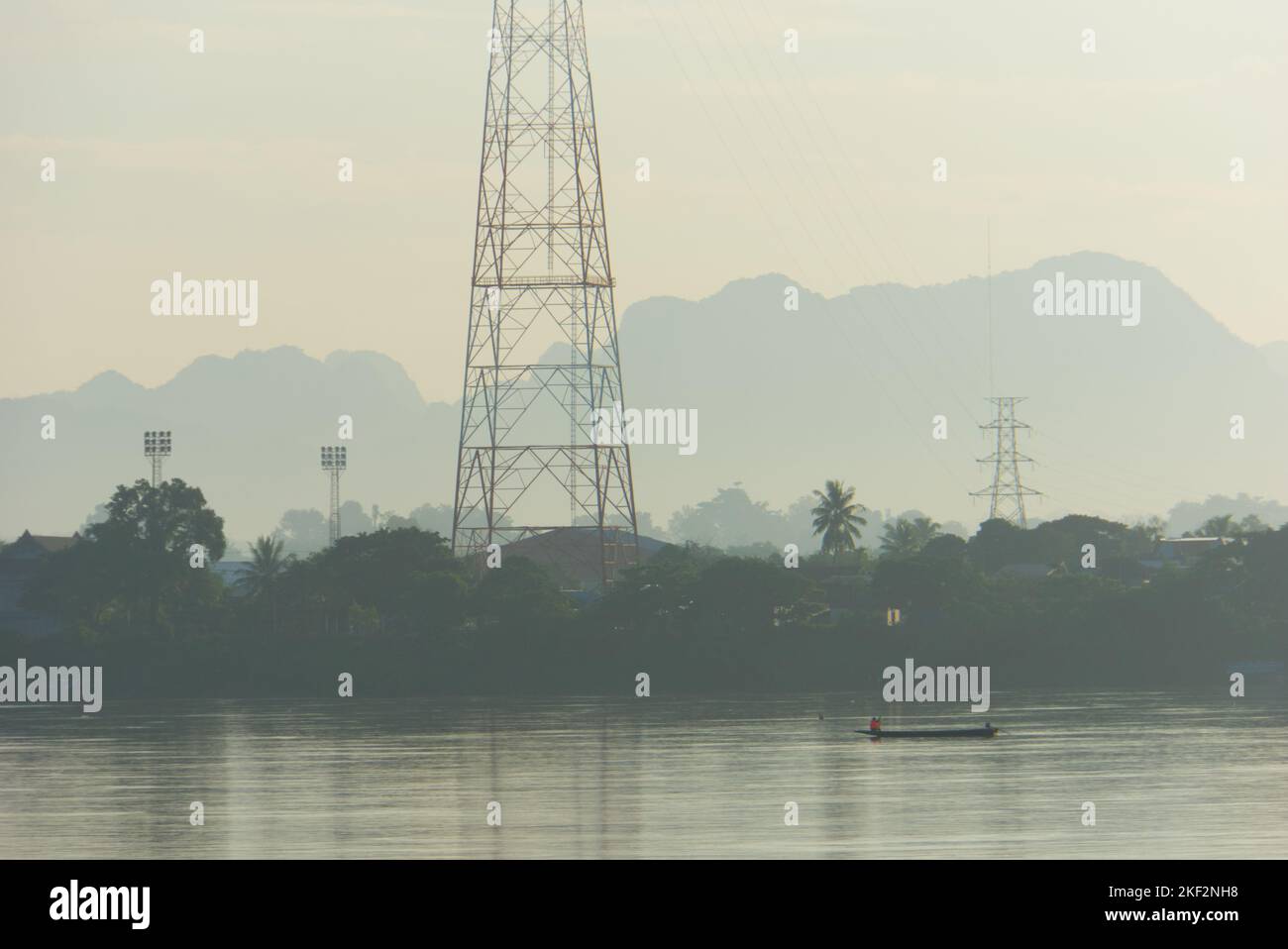 A Mekong river landscape with boat, electricity pylons, buildings and ...