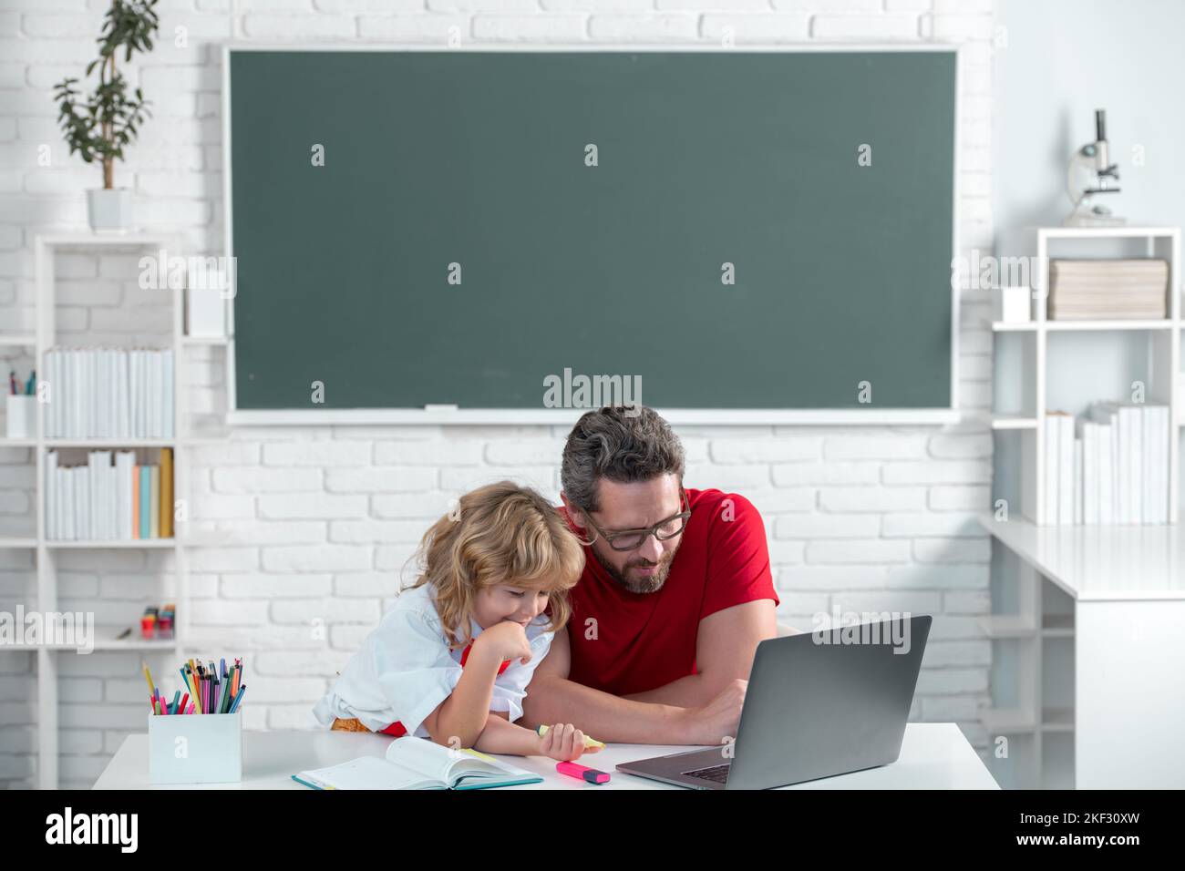 School pupil with teacher learning at laptop computer, studying with ...