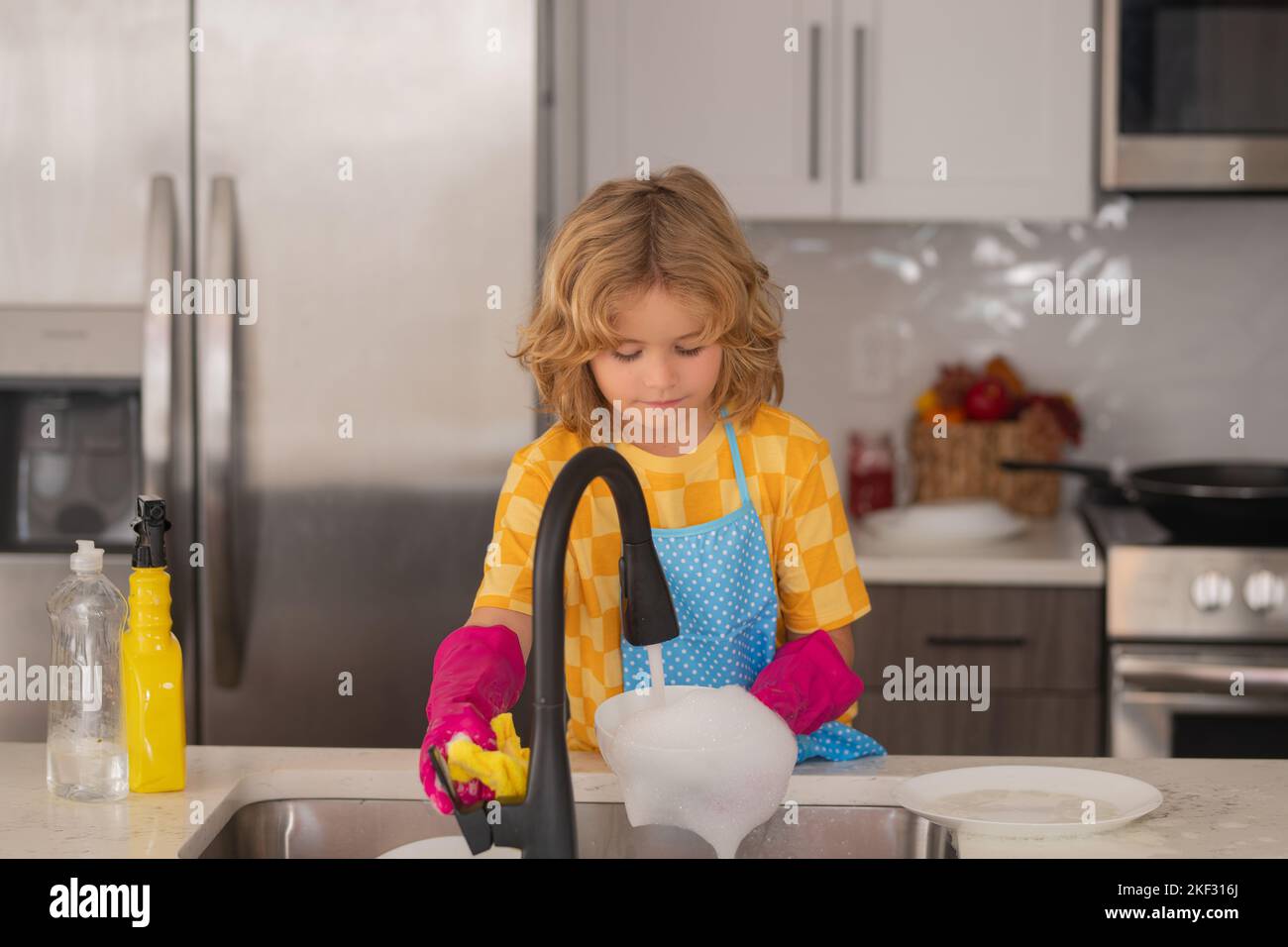Kid washing dishes in the kitchen interior. Child helping with ...