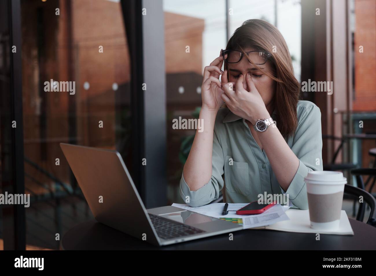 A tired and stressed young woman holds glasses and massages his nose ...