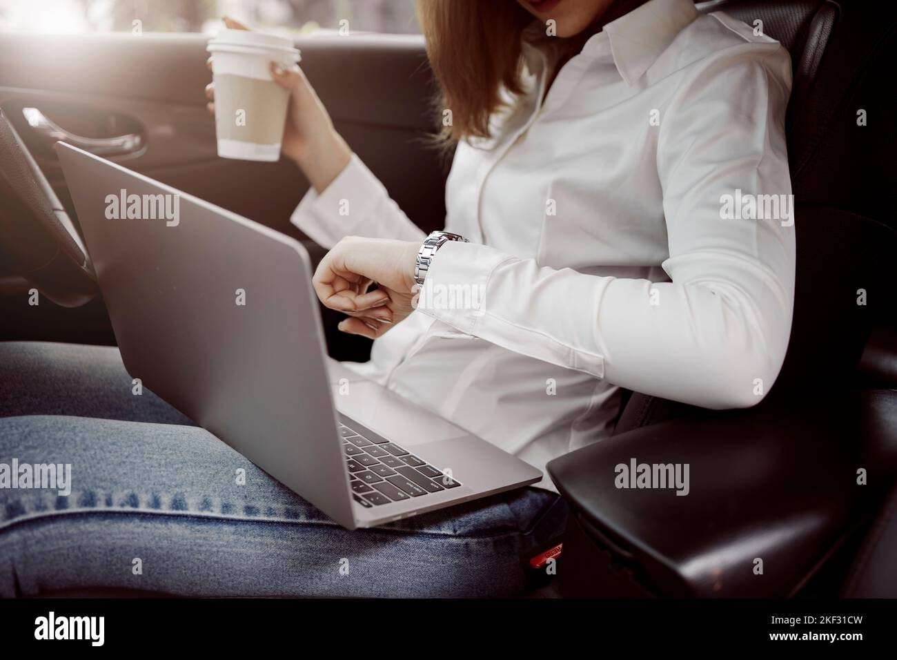 Young woman checking the time on her watch while working on her laptop ...